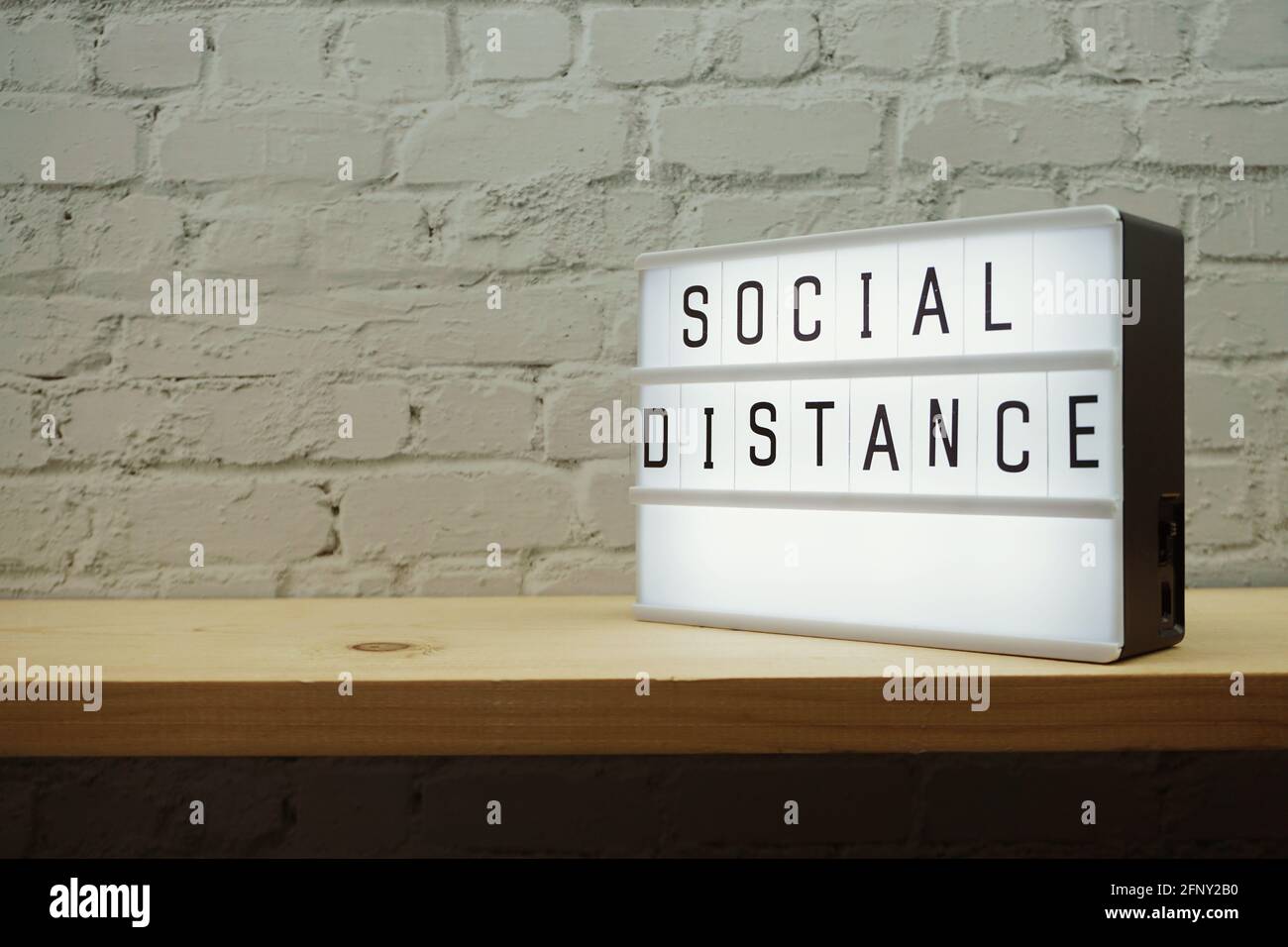 Social Distance word in light box on wooden shelve and white brick wall ...