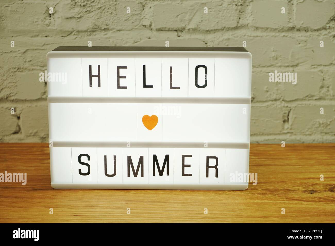 Hello Summer word in light box on white brick wall and wooden ...