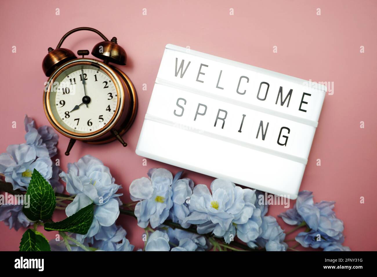 Welcome Spring text in light box and alarm clock with space copy on ...