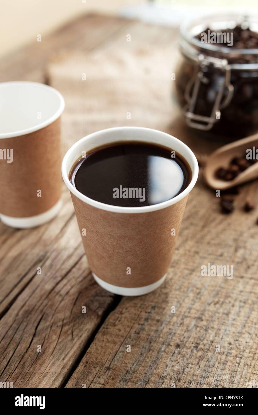 Paper cups of coffee, dry coffee beans in glass jar and spoon at wooden ...