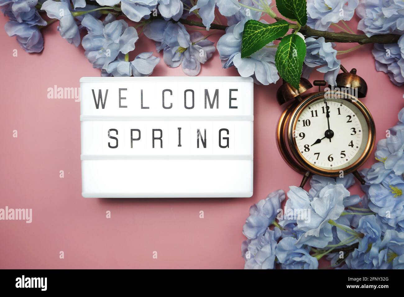 Welcome Spring text in light box and alarm clock with space copy on ...