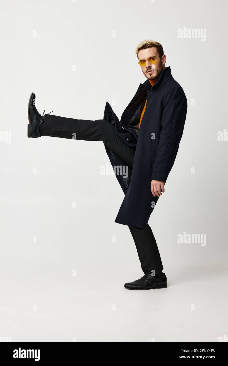 fashionable man in a coat lifted his leg up and glasses on his face ...