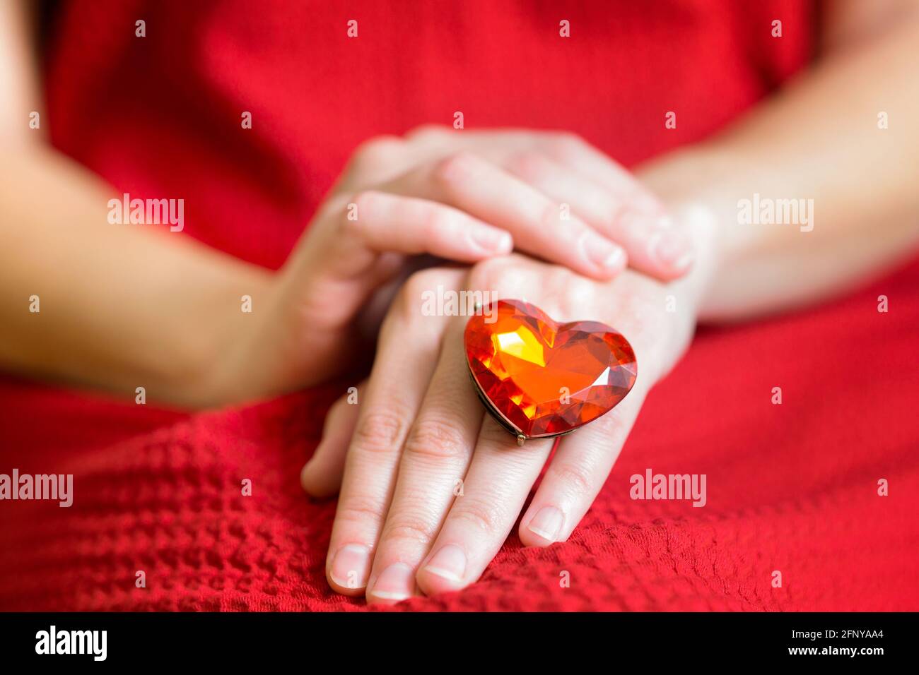 Sitting woman in red wearing a huge heart shaped fake gem stone ring ...