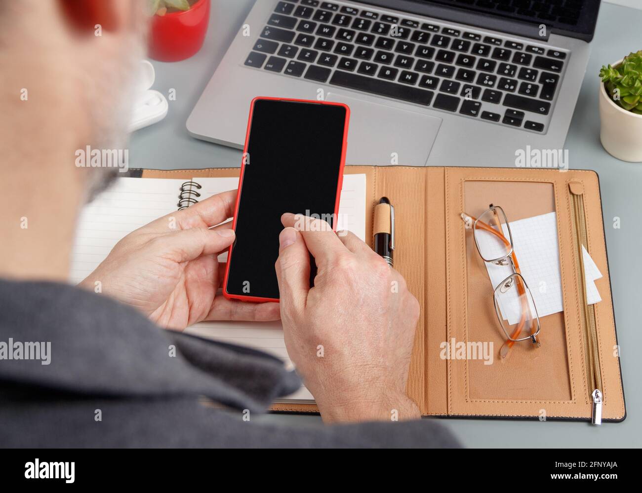 Man writing in agenda and using cell phone on a grey office desk top ...