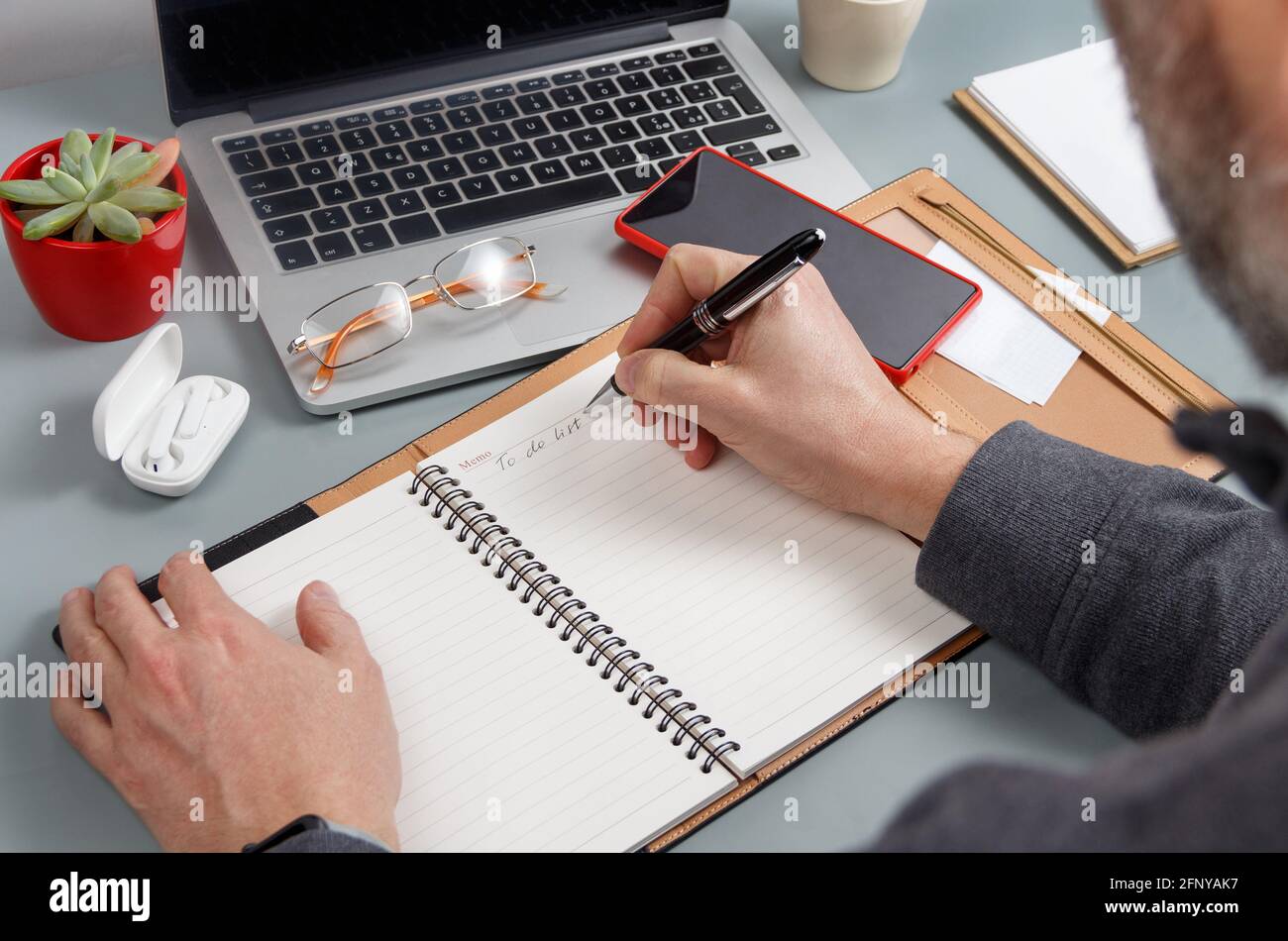 Man writing in agenda TO DO LIST near laptop on a grey office desk ...