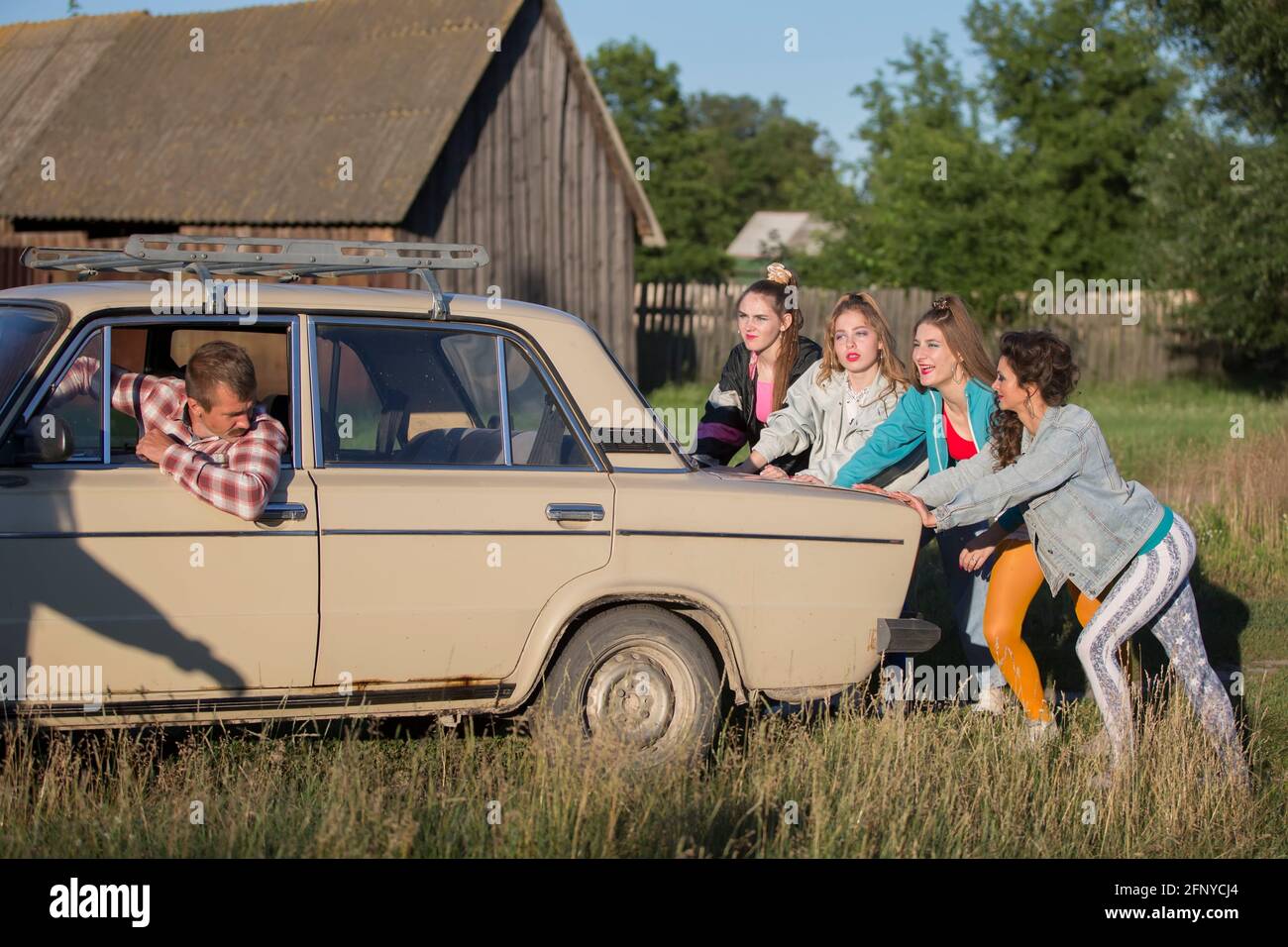 Young cheerful girls are pushing an old car. Women in the style of the ...