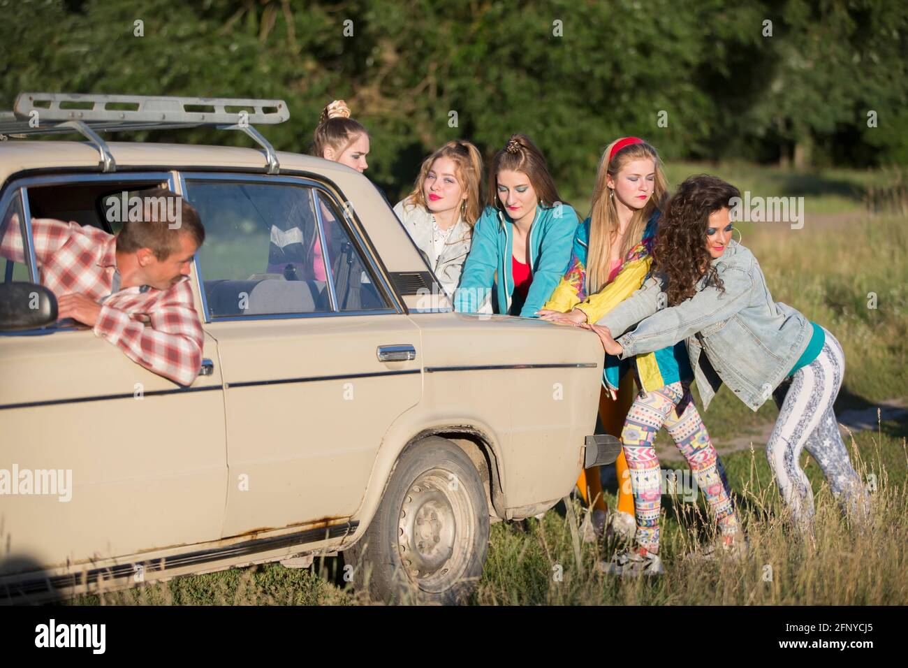 Young cheerful girls are pushing an old car. Women in the style of the ...