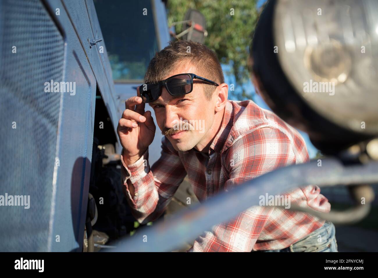 Funny country man repairs a tractor. The man in a shirt in a cage is a ...