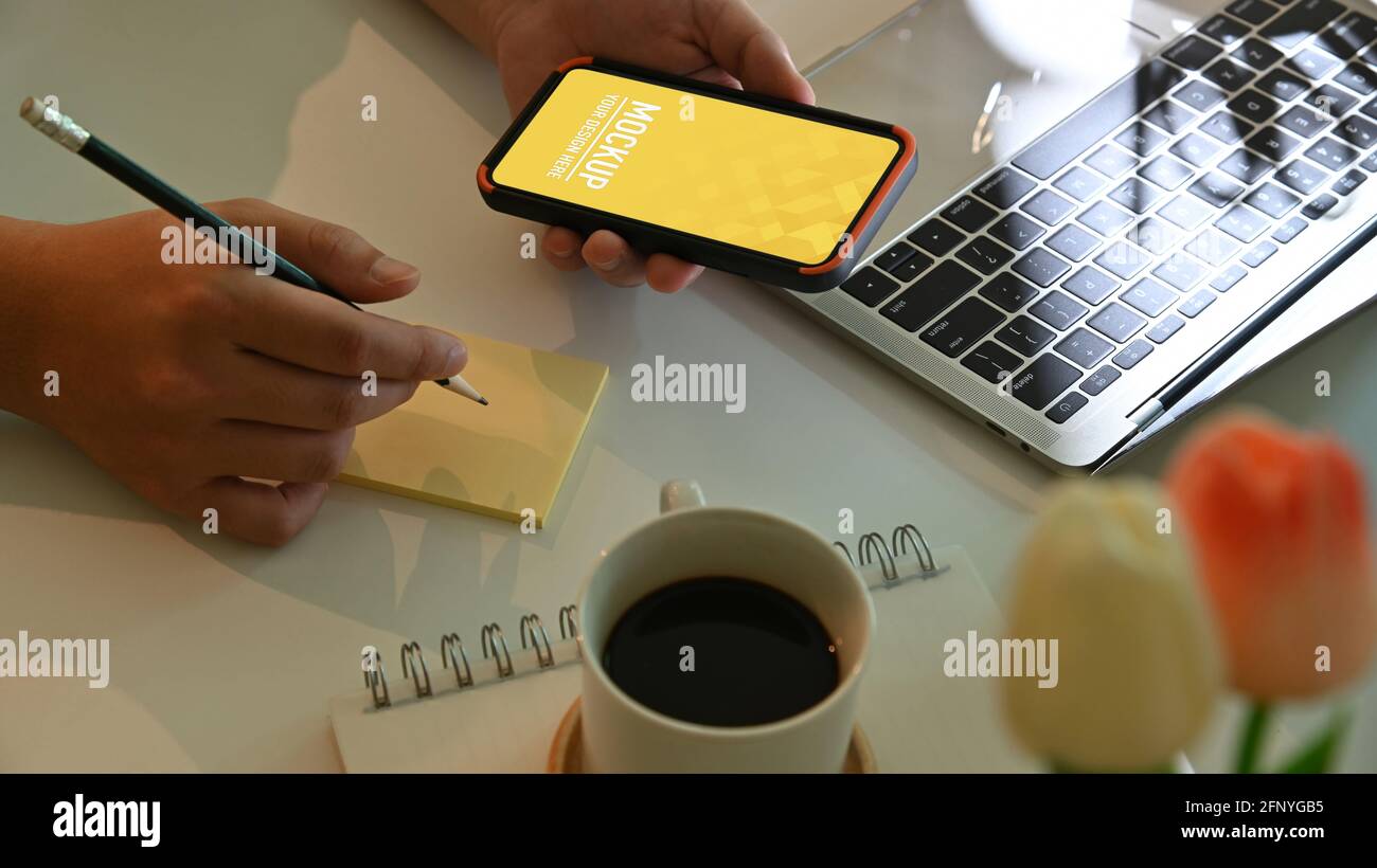 Top view of male hand holding smartphone and taking note on sticky note ...
