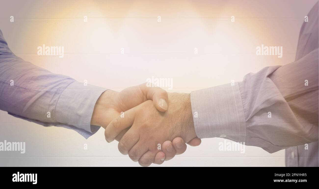 Mid section of two businessmen shaking hands against spot of light ...