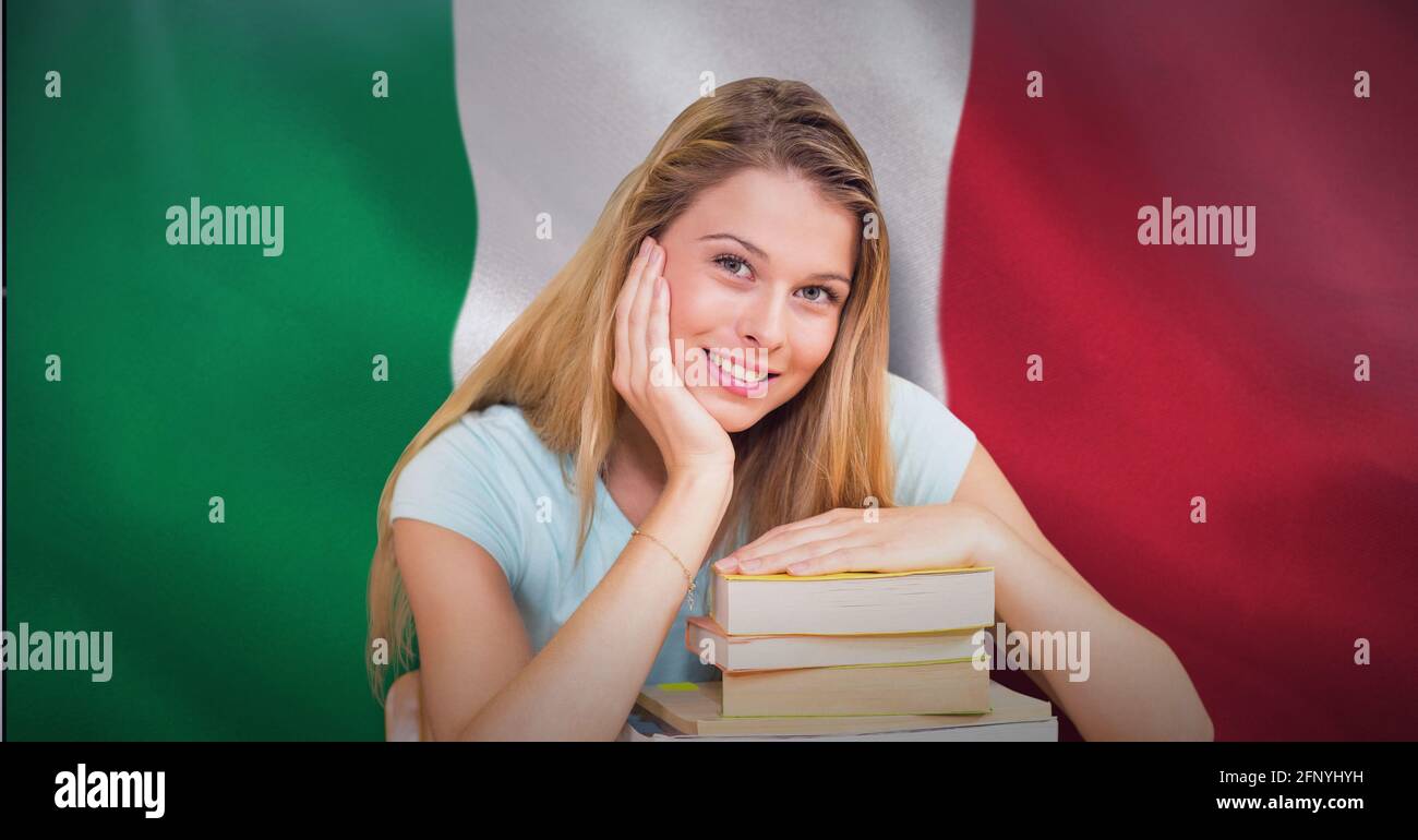Blonde female student smiling with stack of books over italian flag ...