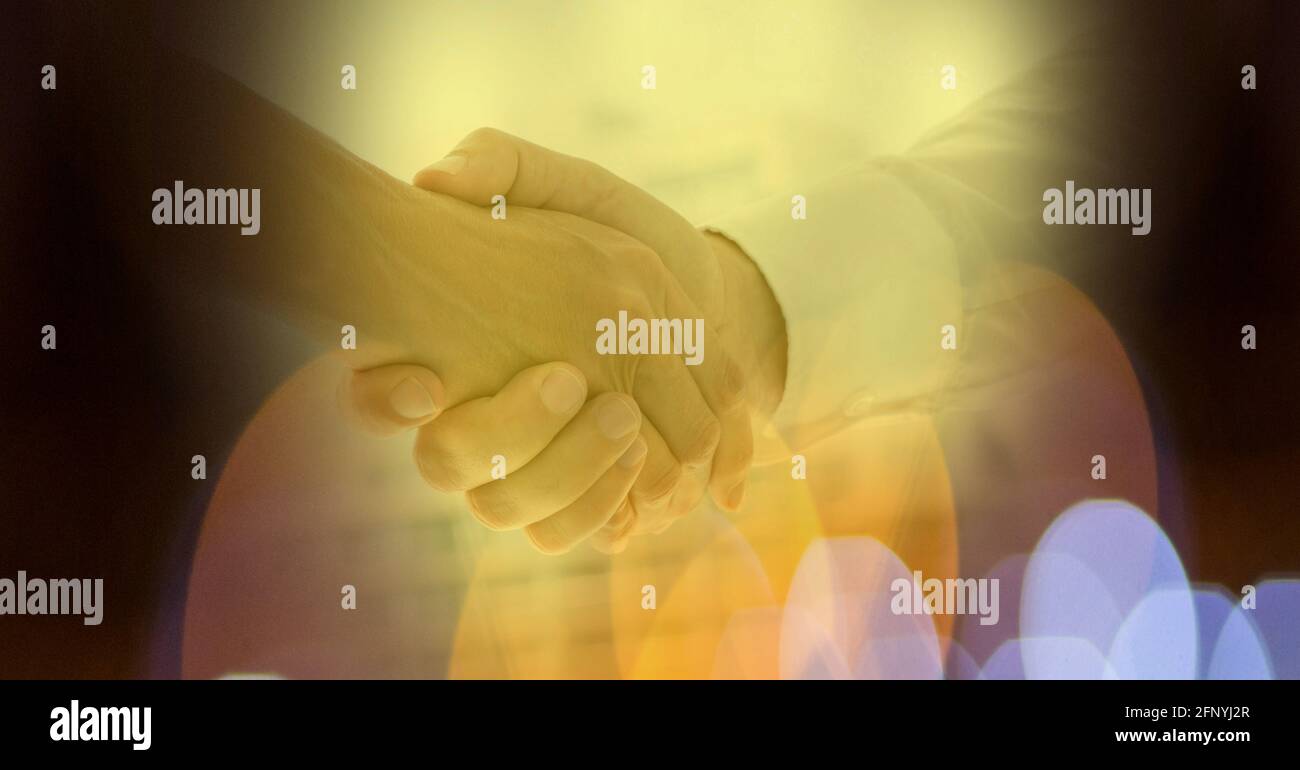 Composition of businessman handshake with glowing yellow spots of light ...