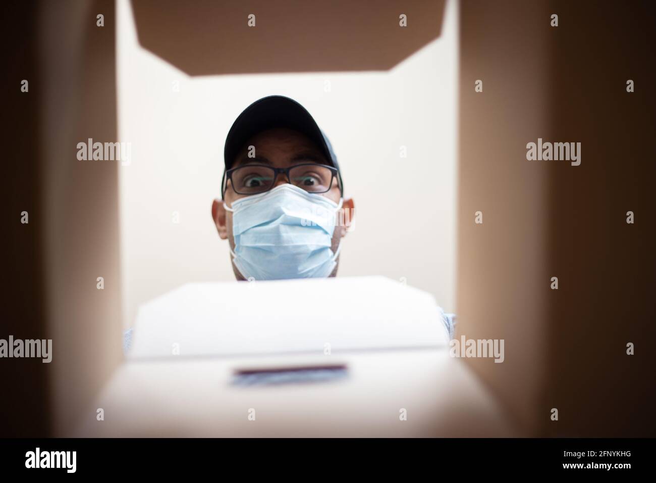 Surprised male in a face mask opening a home delivery box; new normal ...