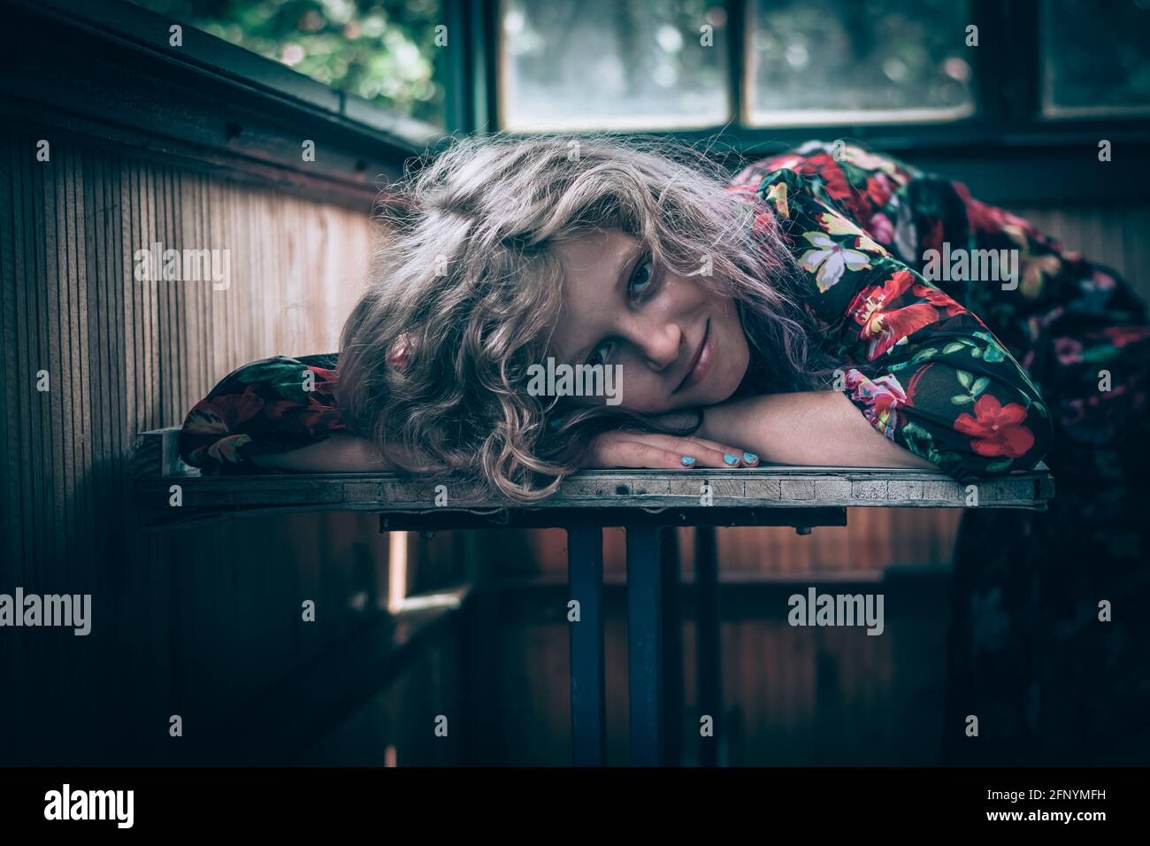 adorable girl with long blond hair lying on the table next to window ...