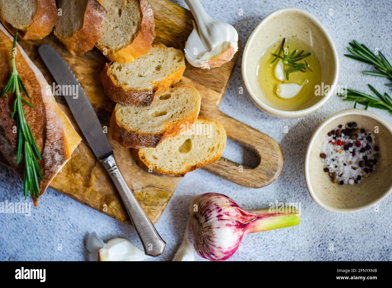 Overhead view of sliced baguette loaf with a bowl of olive oil, garlic ...