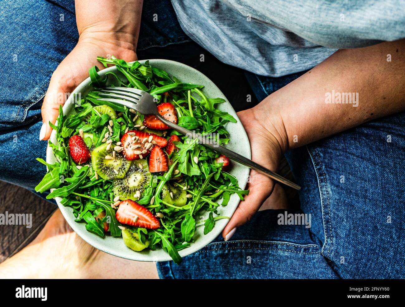 Close-up of a woman eating a bowl of rocket, strawberry and kiwi fruit ...