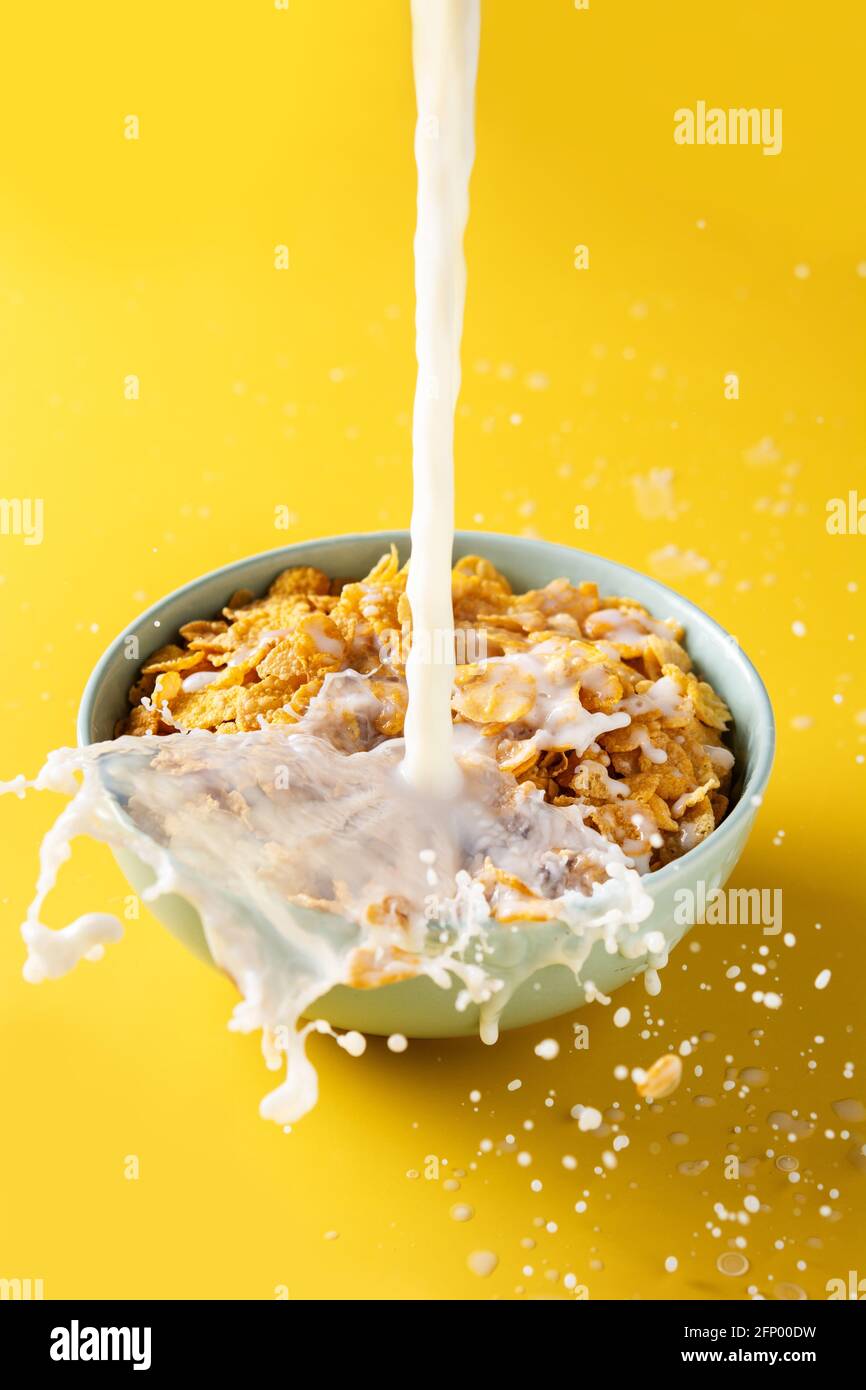 Pouring milk into bowl of corn flakes on yellow background Stock Photo ...