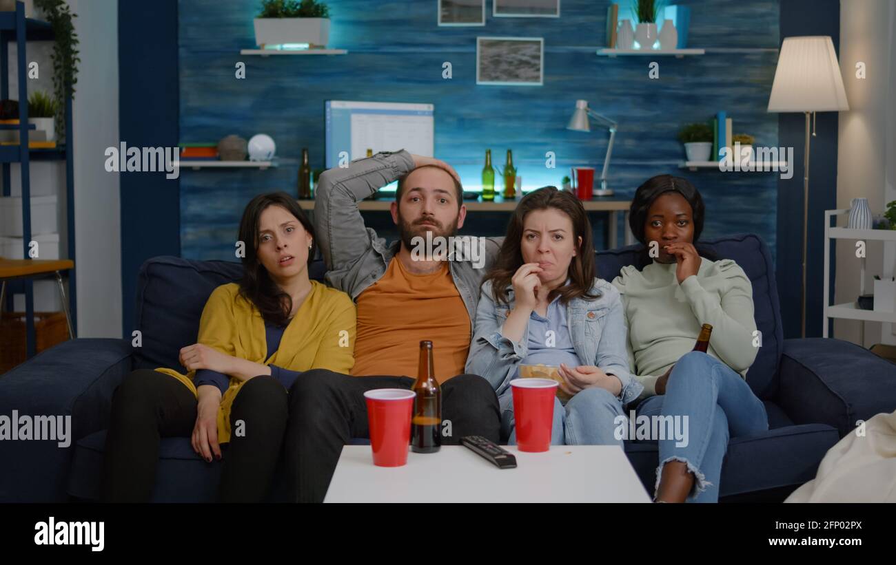 Group of mixed race people watching horror filme on television ...
