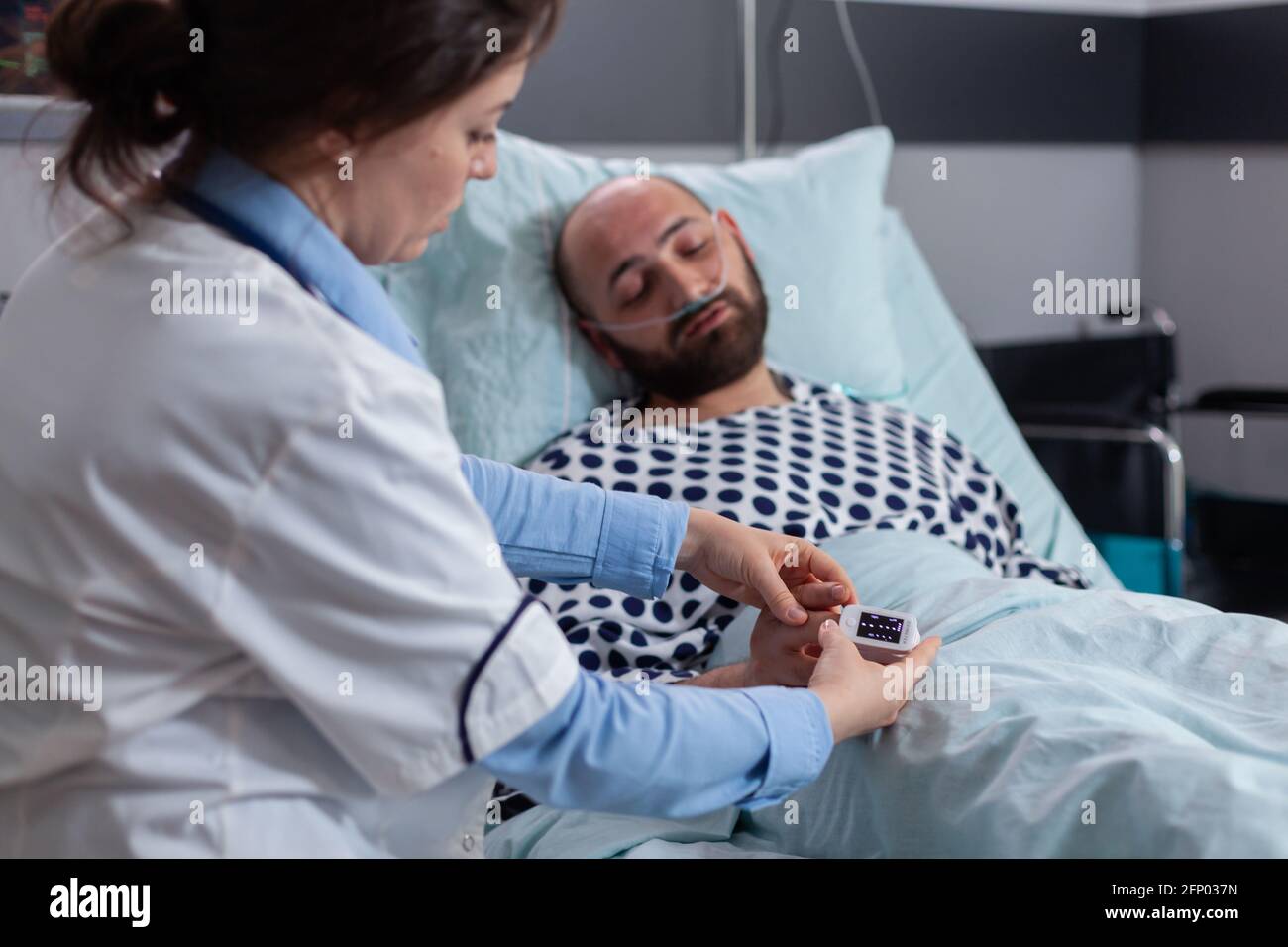Close up of sick man patient lying in bed with medical oximeter on finger. Woman doctor ...