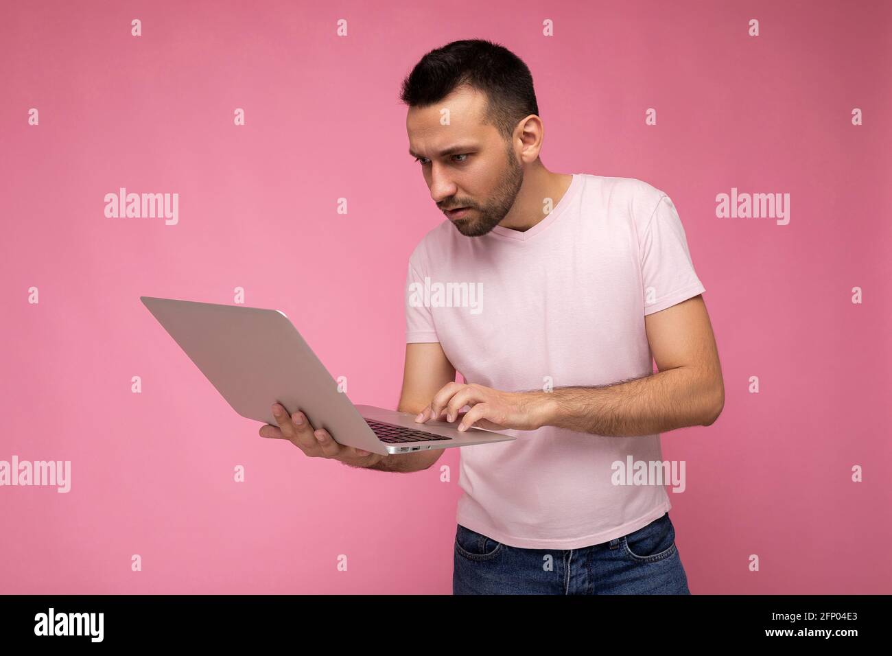 Handsome brunet man holding laptop computer and typing on the keyboard ...