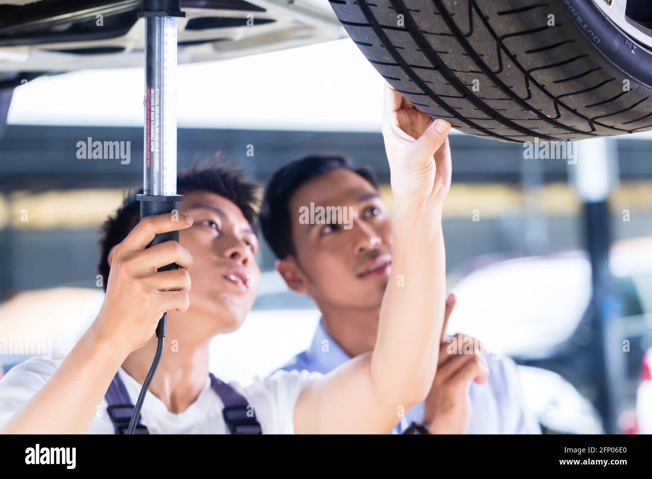 Asian Chinese car mechanic with customer looking at auto floor with ...