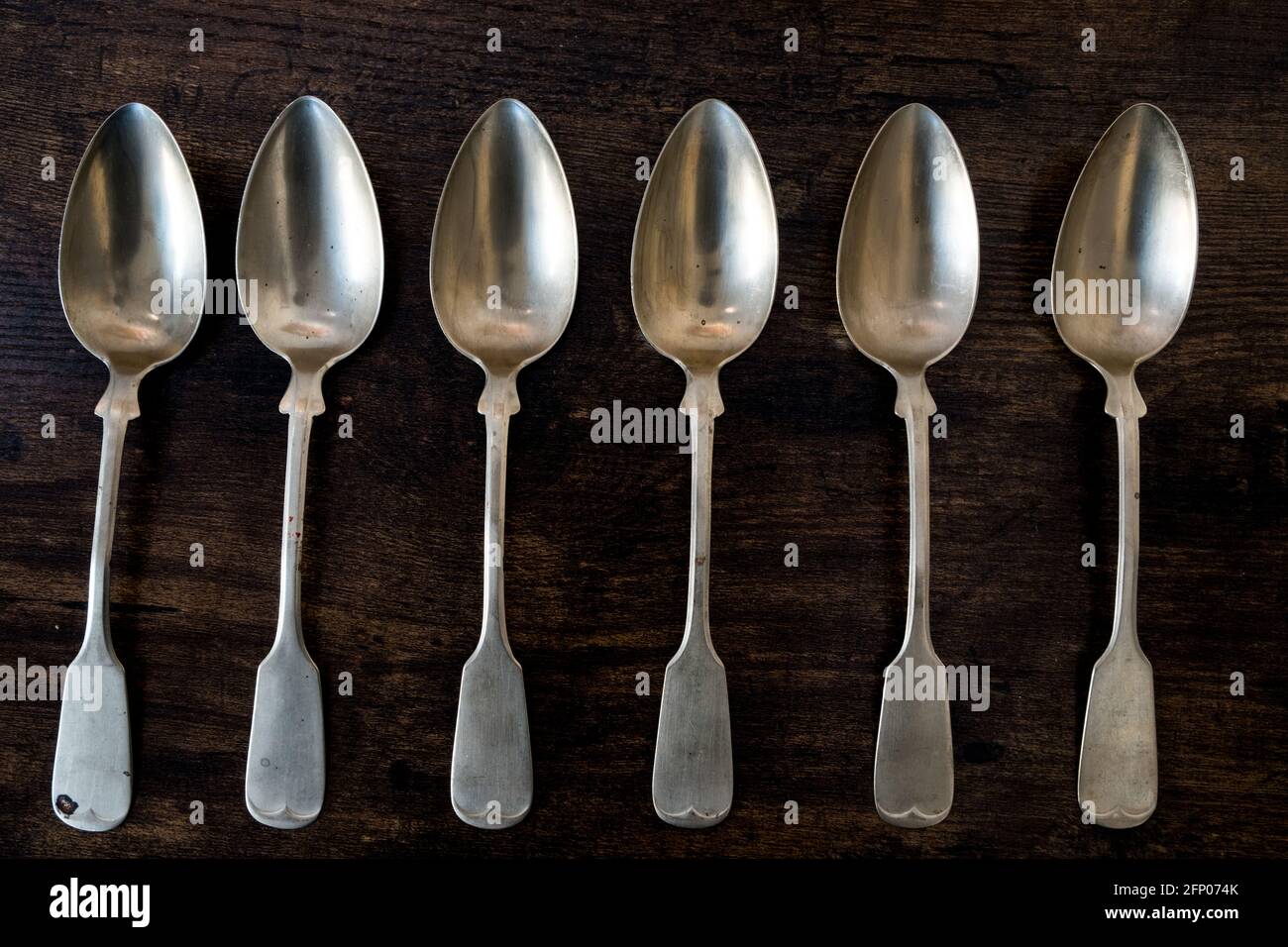 six silver spoons lying in a row on wooden table Stock Photo - Alamy