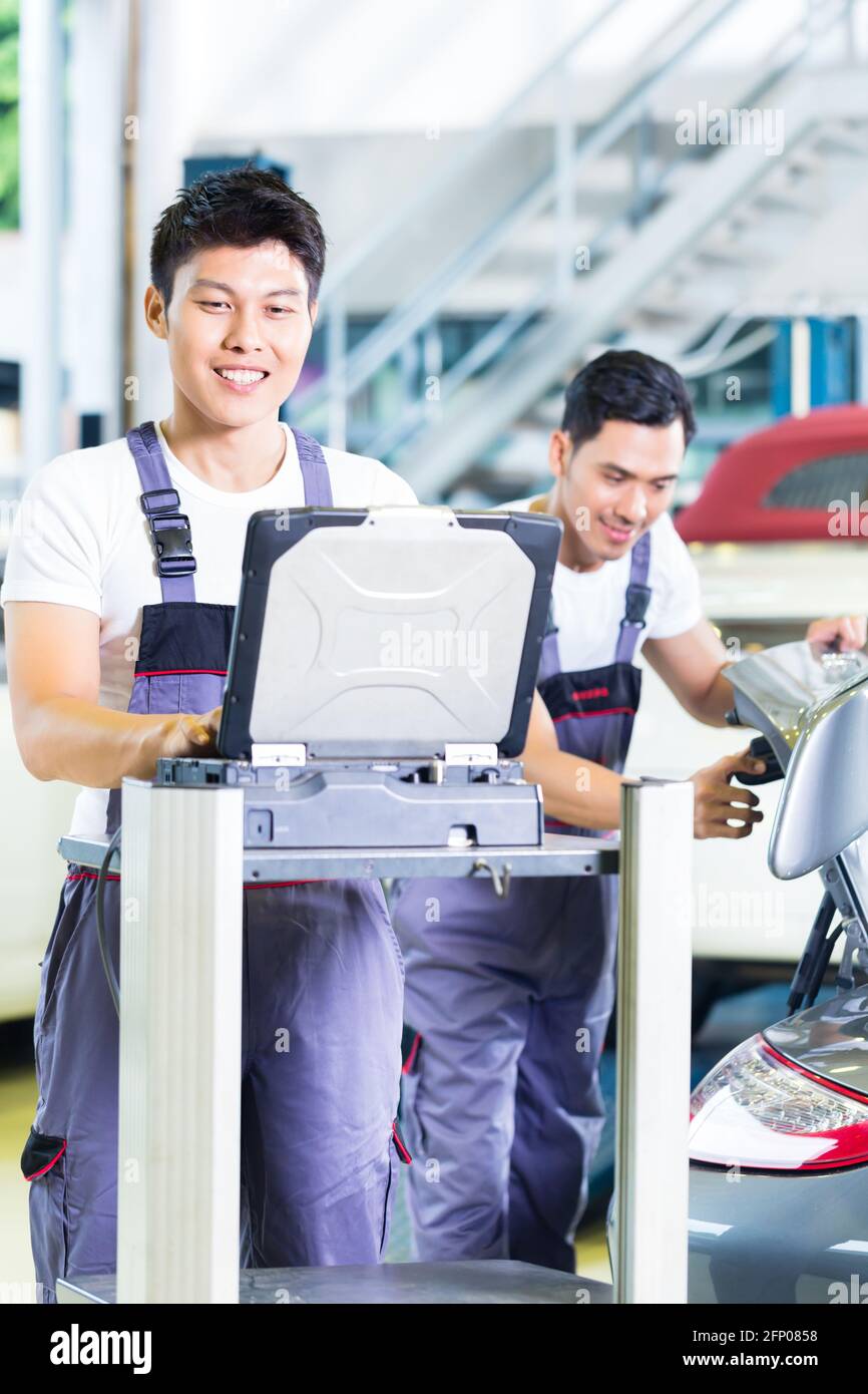 Asian Chinese car mechanics checking auto engine with diagnostics tool ...