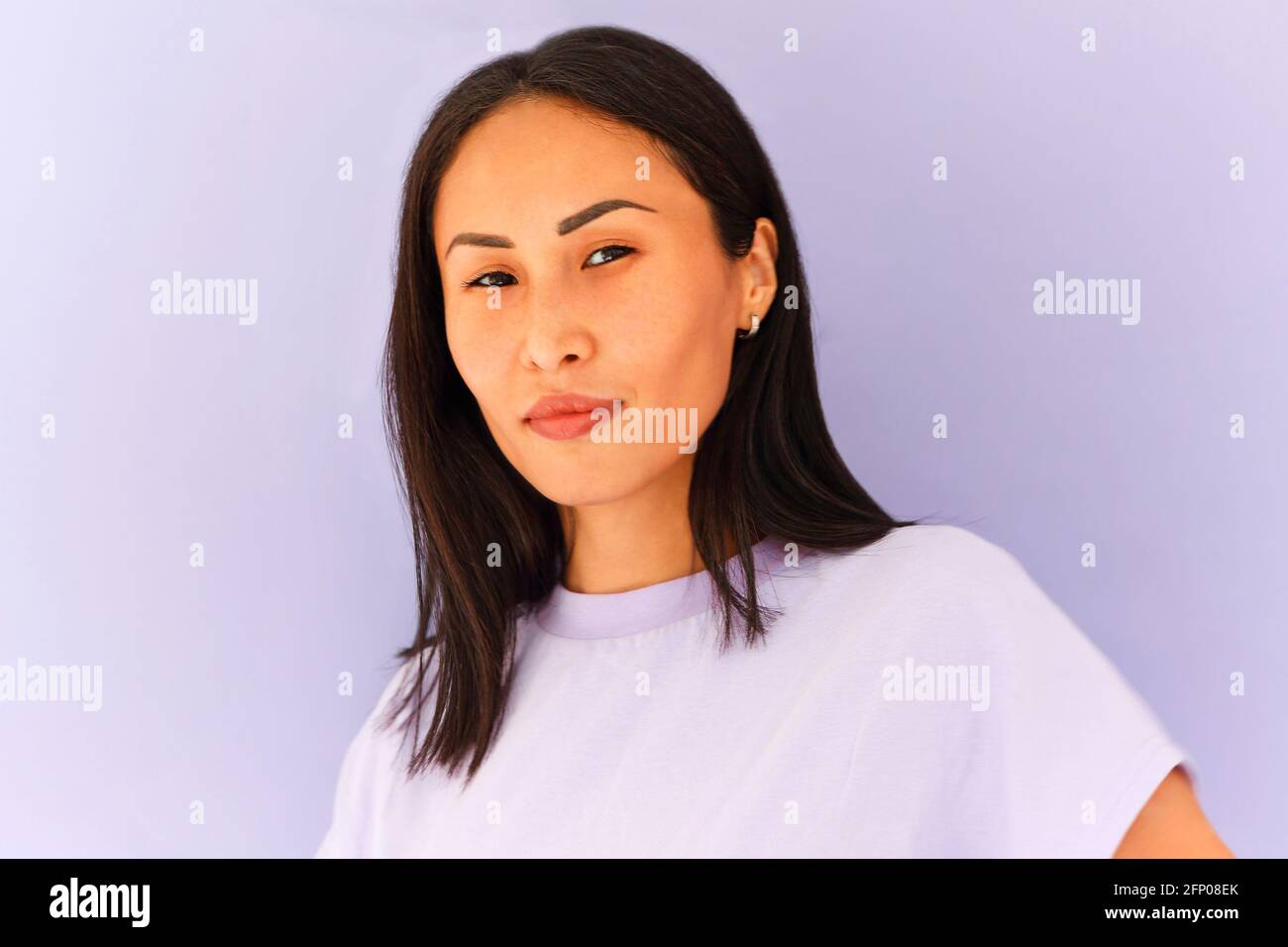 Positive millennial Asian female in casual shirt in light violet studio ...