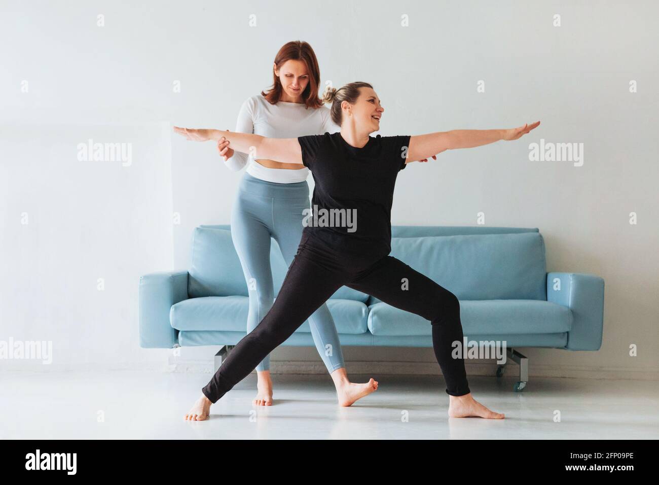 Adult woman helping female in sportswear with doing yoga pose and ...