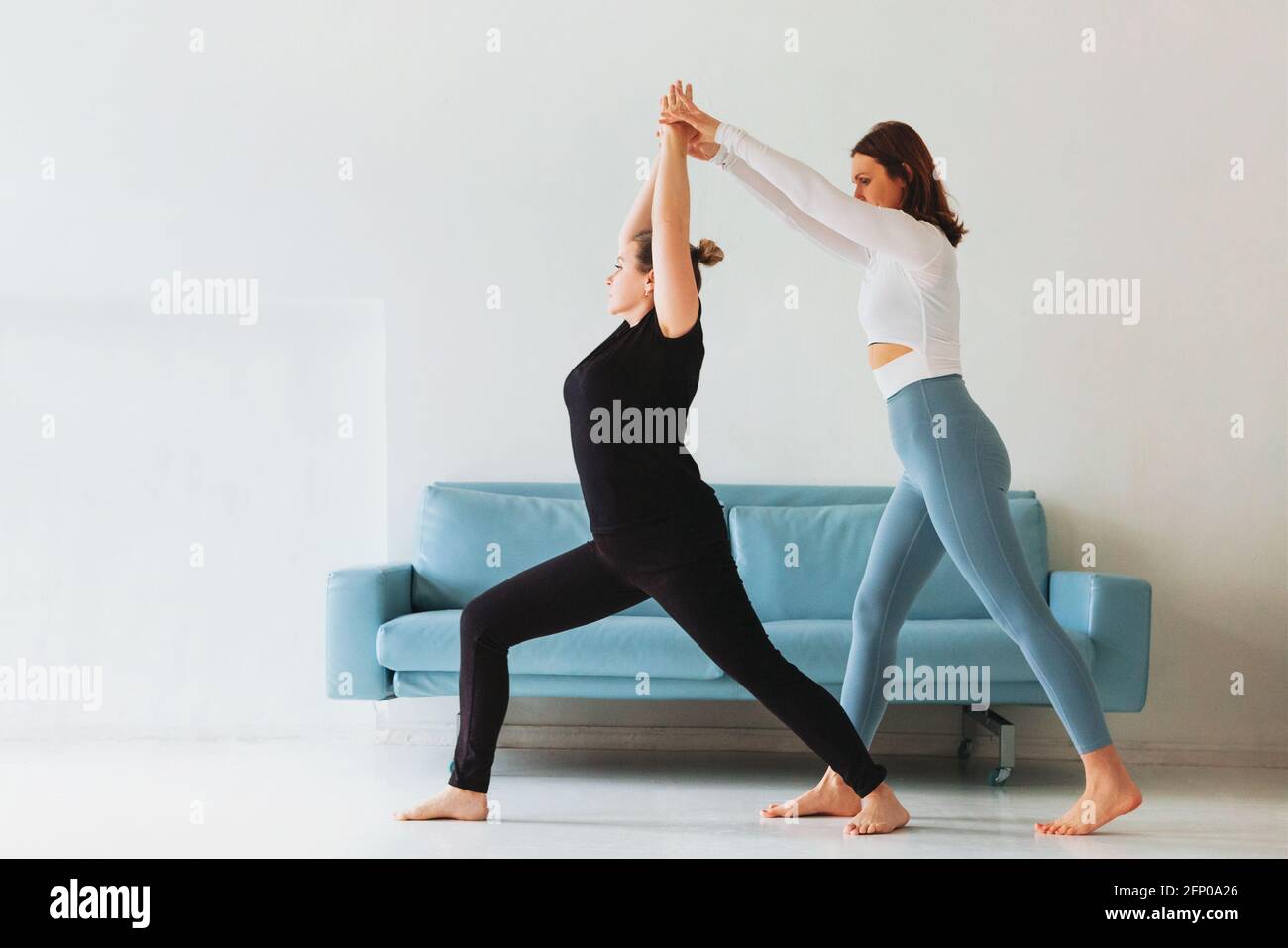 Adult woman helping female in sportswear with doing yoga pose and ...