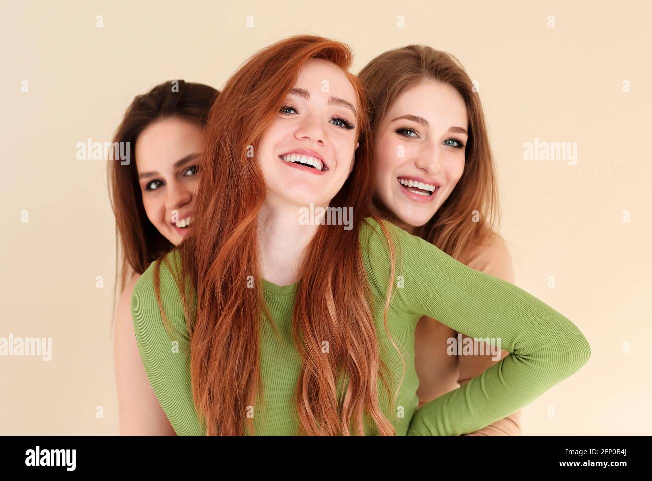 Cheerful young girlfriends smiling and looking at camera while hugging ...