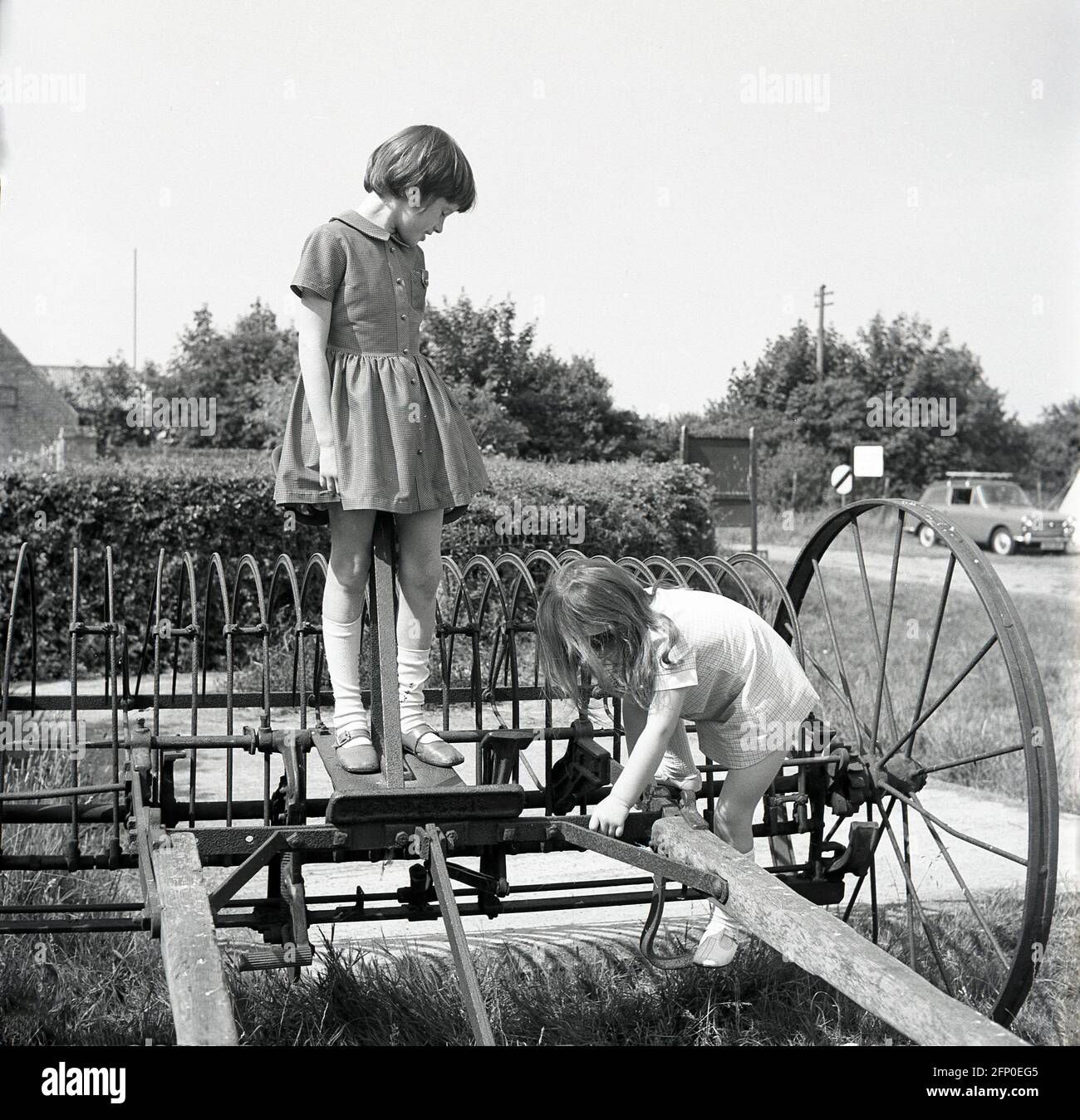 1960, historical, two young girls playing on an old agricultural, steel ...