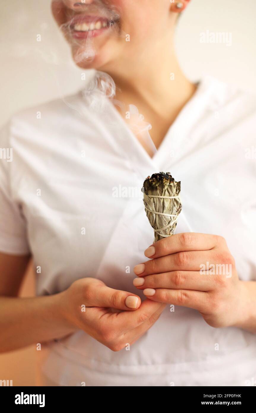 Unrecognizable female burning sage smudge stick and smelling smoke ...