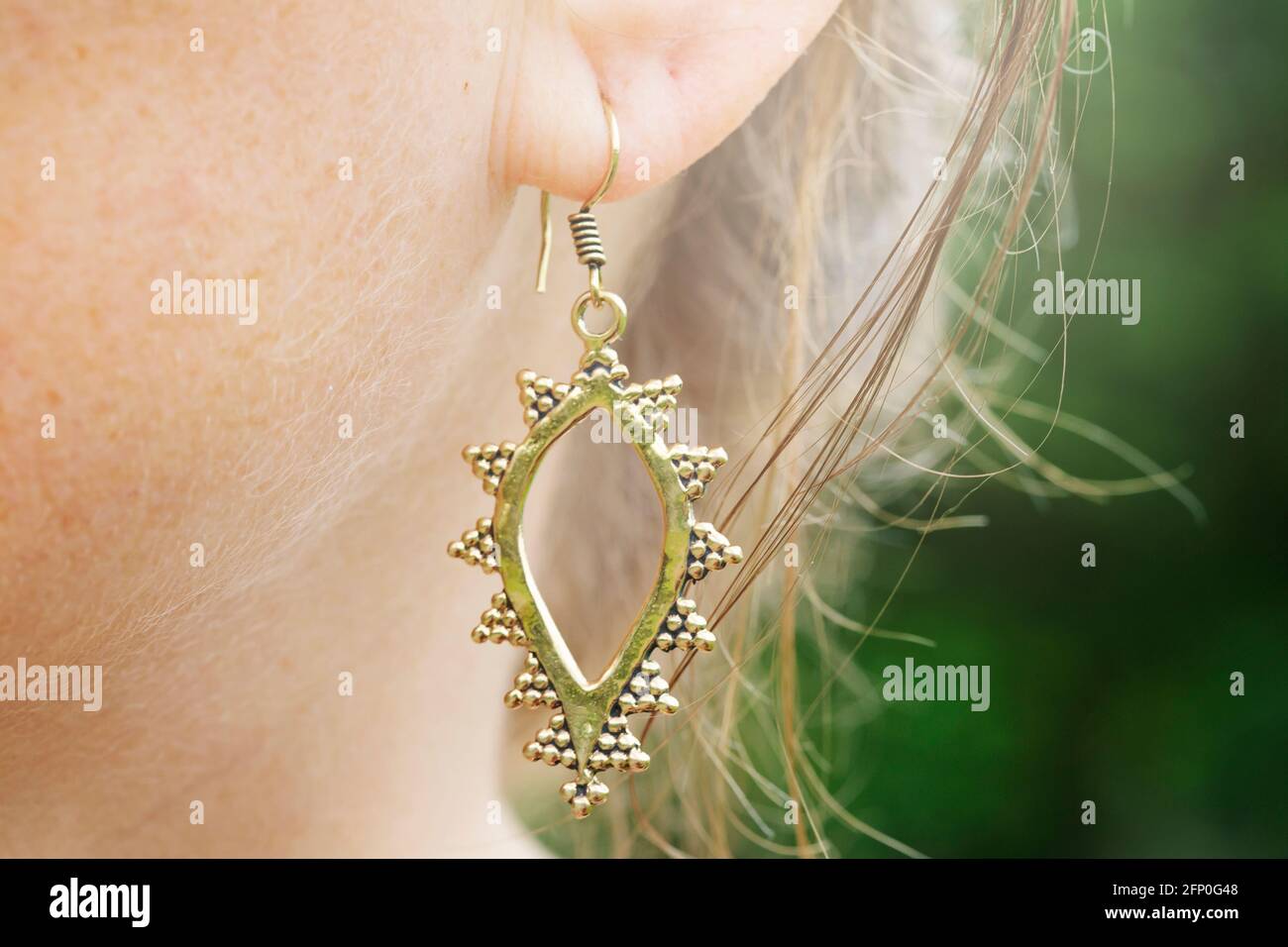 Outdoor detail of female ear wearing metal decorative shape earring ...