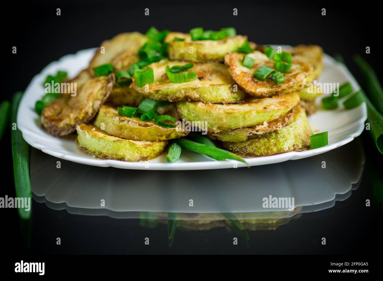 fried zucchini in circles with fresh herbs in a plate on a black Stock ...