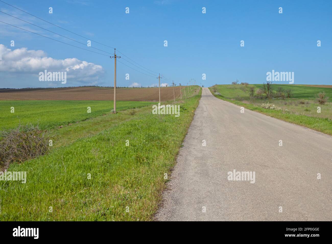 The asphalt road borders a plowed and green field. The background is ...