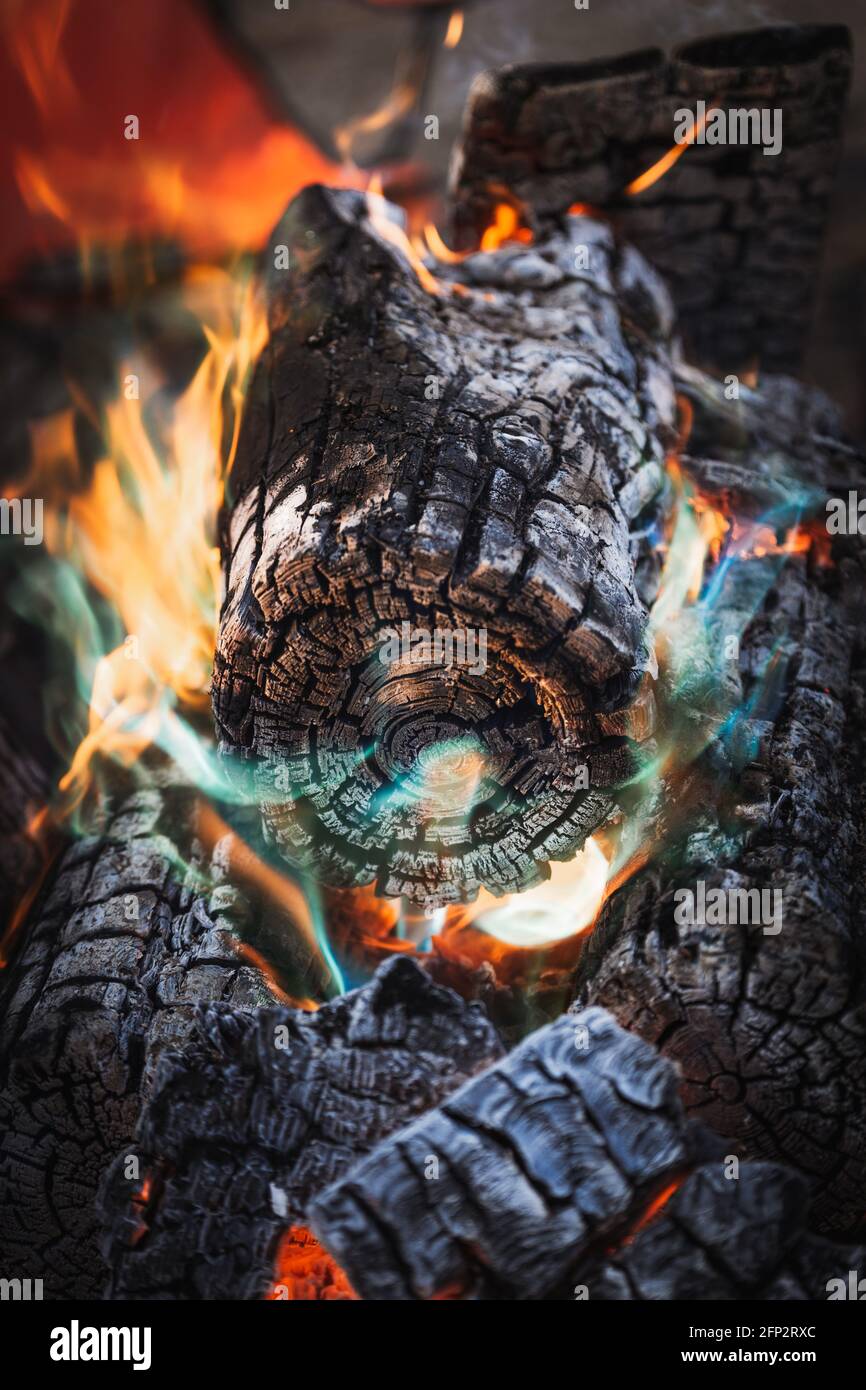 Multi colored flames engulfing black charred logs in a ...