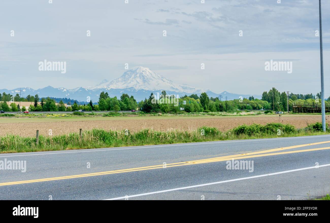 A view of a road, a field and Mount Rainier in Kent, Washington Stock ...