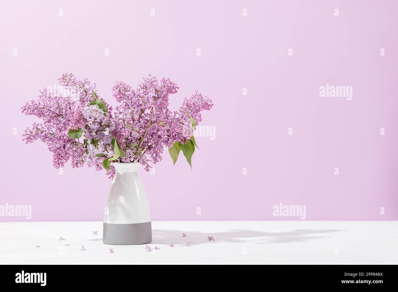 Vase with fresh blooming lilac flowers standing on table against ...