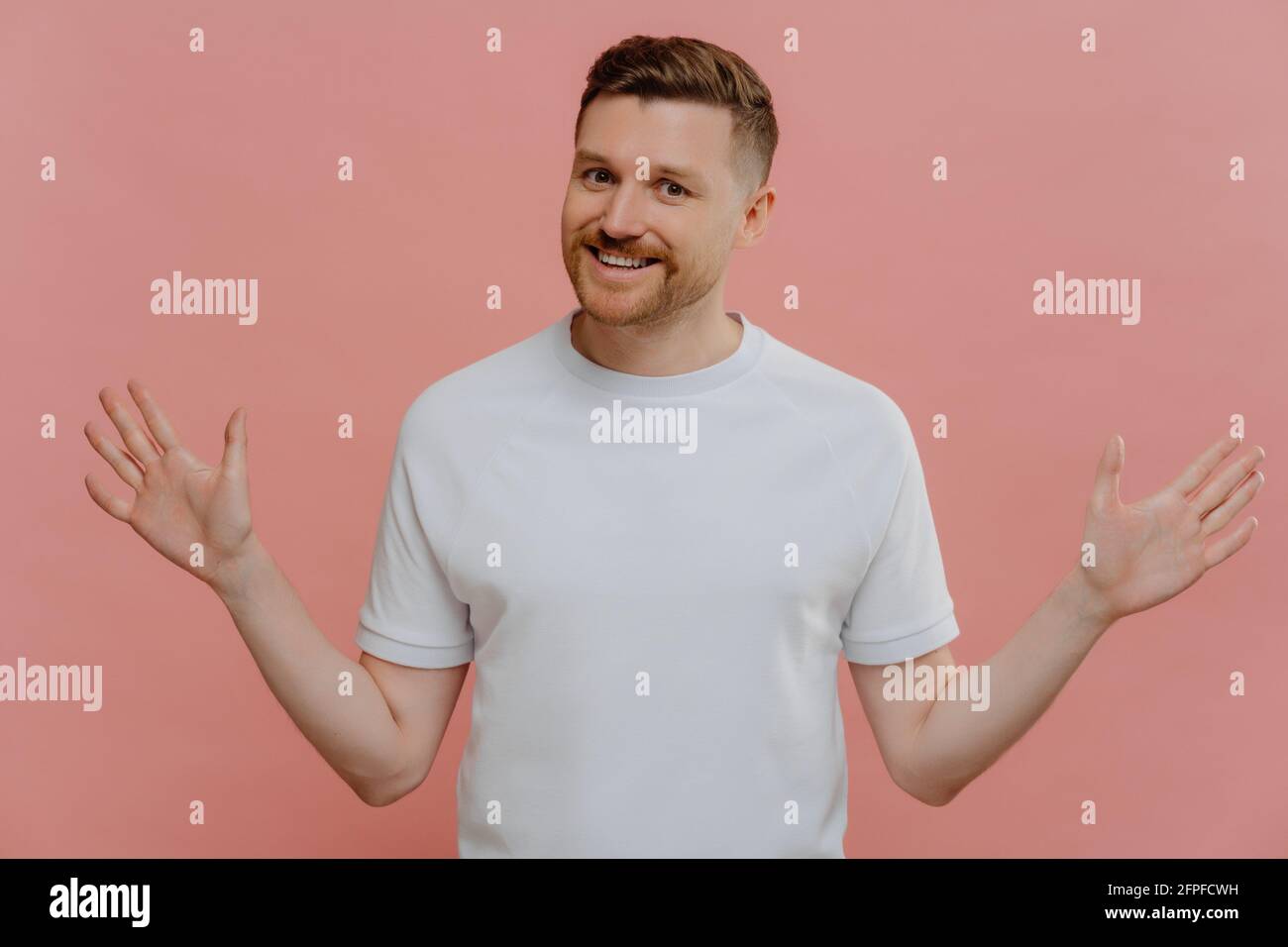 Happy young man spreading hands sideways while posing against pink ...