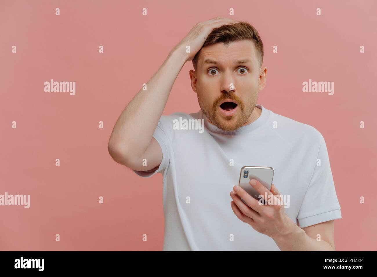 Amazed young man holding smartphone and looking at camera with shocked ...