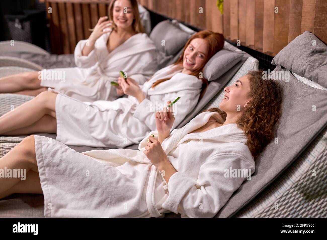 Young women putting cucumber slices on eyes. Young caucasian ladies in ...