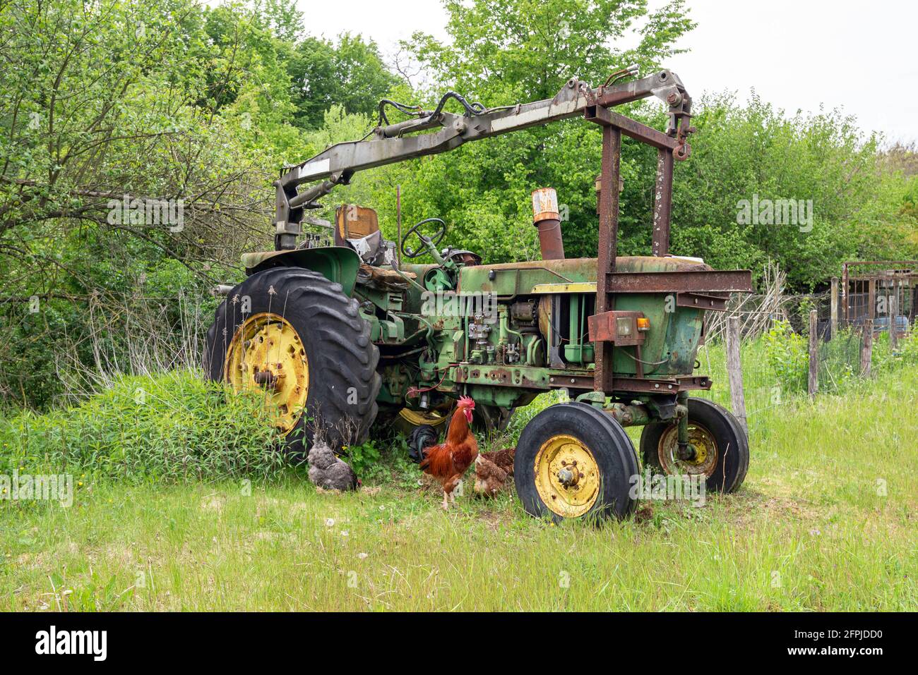 Old rusty tractor abandoned in a field overgrown with tall grass and ...