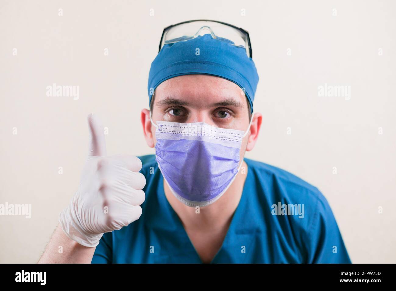 Young doctor portrait with thumb up in blue surgeon suit and glasses on ...