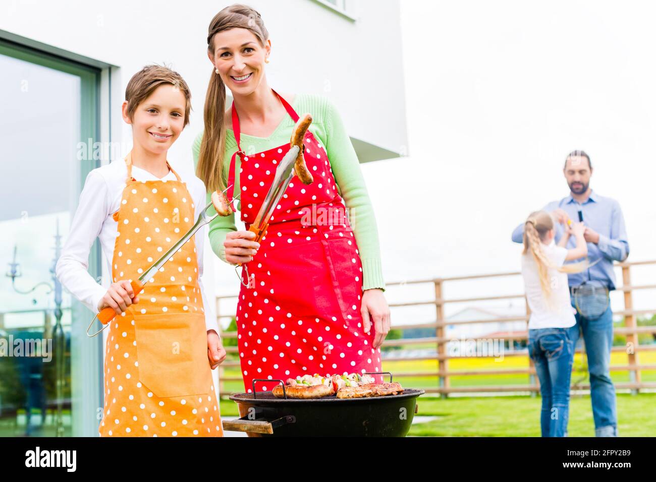 Mother and Son barbecue meat spits and sausages at family garden BBQ ...