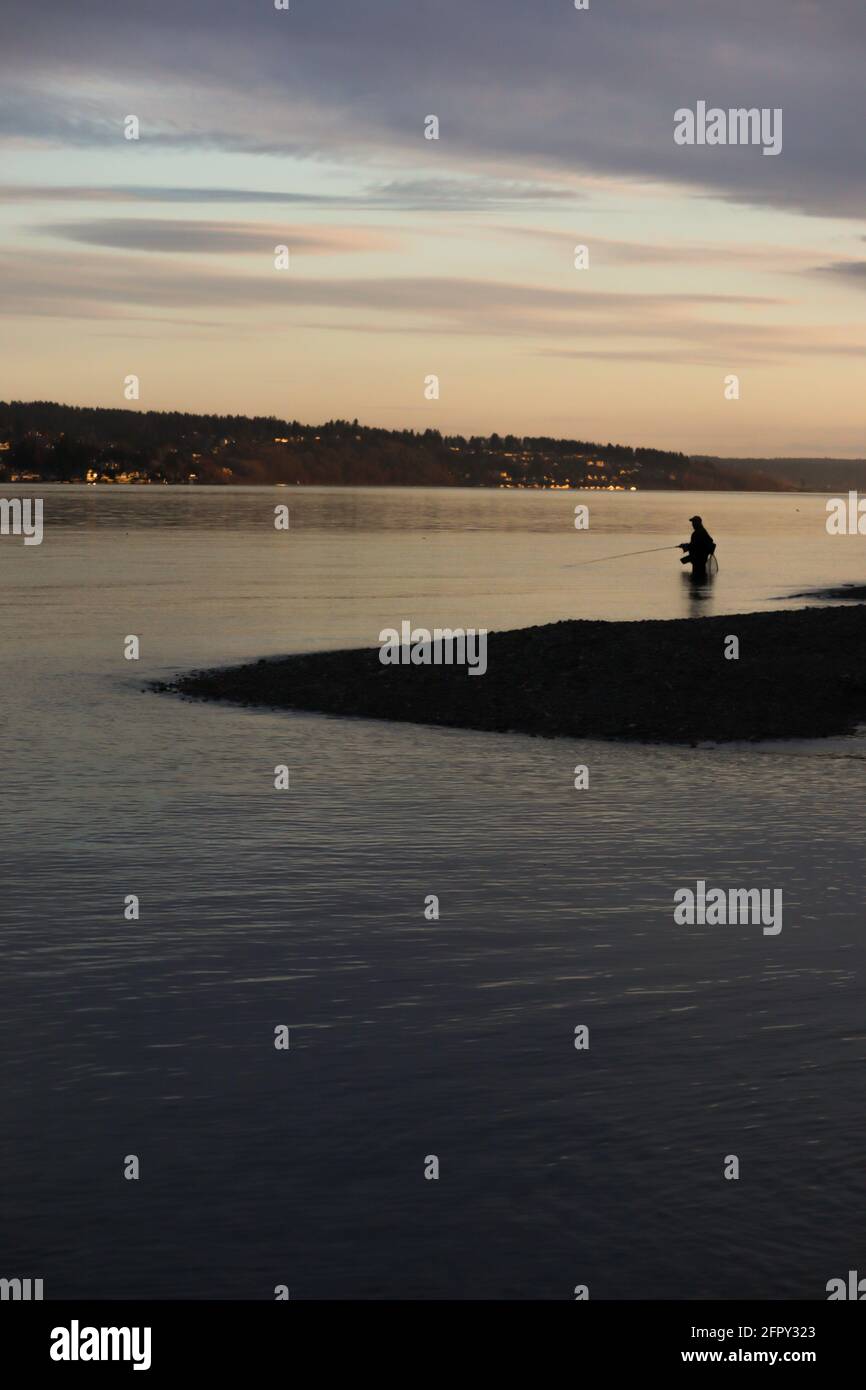 A man wading into water with fishing pole and gear at sunset Stock ...