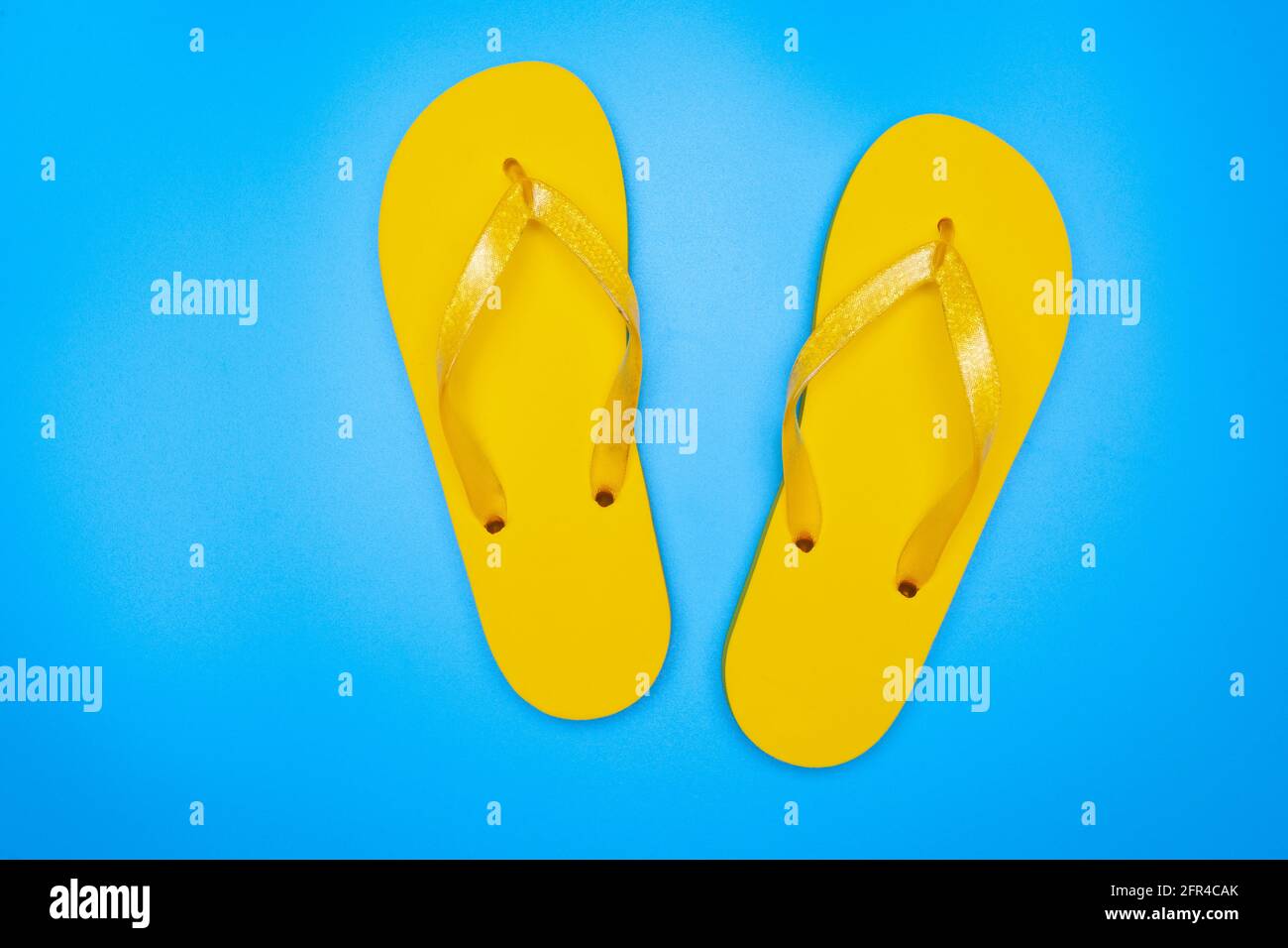 yellow rubber flip-flops isolated over blue background, pair of thongs ...