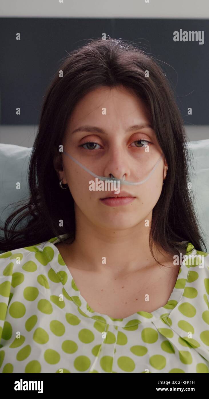Portrait of sick woman wearing nasal oxygen tube resting in bed ...