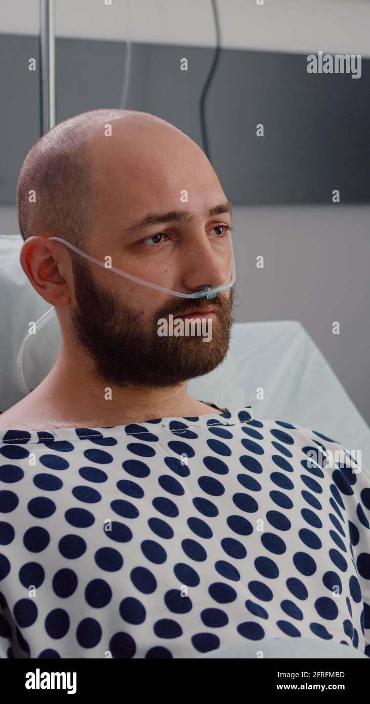 Sad sick man with nasal oxygen tube resting in bad looking into camera ...