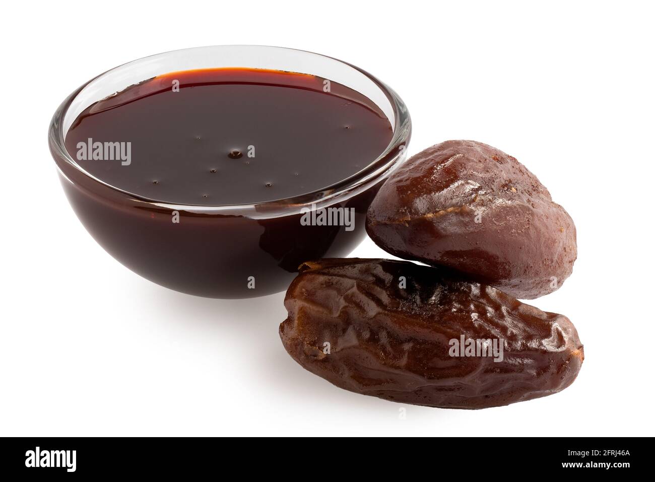 Date syrup in a glass bowl next to two whole dry pitted dates isolated ...